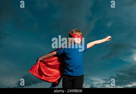 Superhero kid against dramatic blue sky background. Strong super hero ...