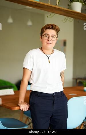 Transgender professional stands confidently in an office with laptop ...