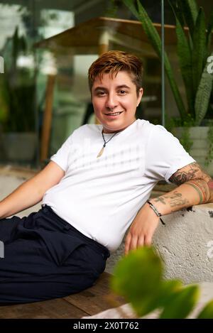 Smiling Gen Z transgender office worker in smart casual clothes sits on ...