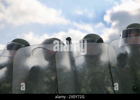 Riot police forming a line carrying perspex shields and wearing helmets ...