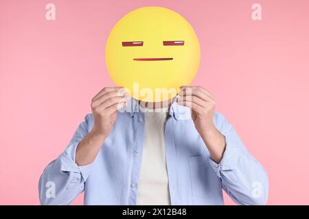 Man holding emoticon with closed eyes and mouth on pink background ...