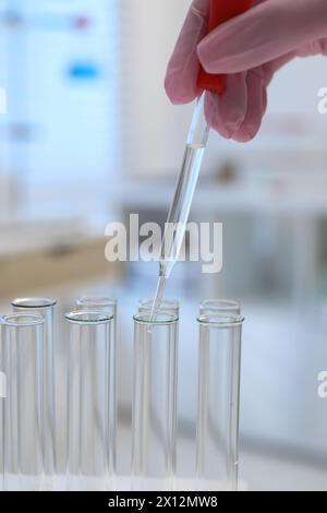 Laboratory analysis. Woman dripping liquid into test tubes at white ...