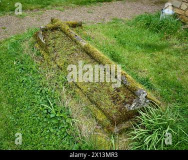 Ancient grass and moss covered cross shaped carved gravestone Stock ...