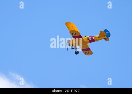 A yellow old style biplane soars up in the bright blue sky near Liberty ...