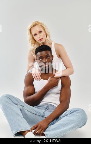 A young man and woman sit intertwined on a chair, their gazes locked in ...