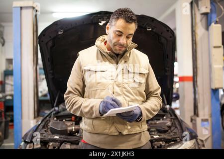 mechanic takes notes while checking levels of vehicle in mechanical ...