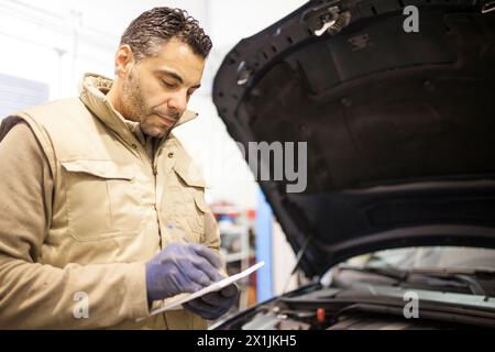 mechanic takes notes while checking levels of vehicle in mechanical ...