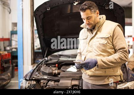 mechanic answers a phone call while checking vehicle levels in a ...