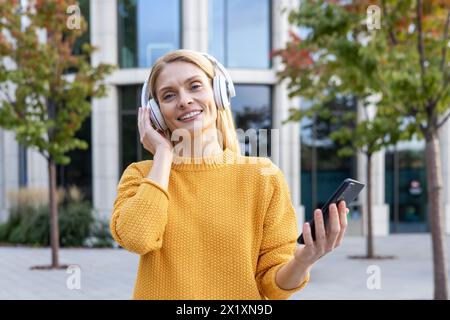 A cheerful blonde woman enjoys music while showcasing her stylish denim ...