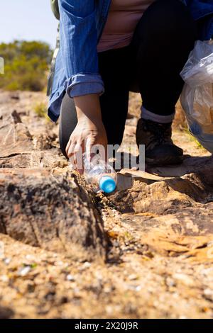 Biracial female hiker picking up trash on mountain trail adventure in ...