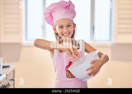Portrait of baker girl in hat and apron next to display case of fresh ...