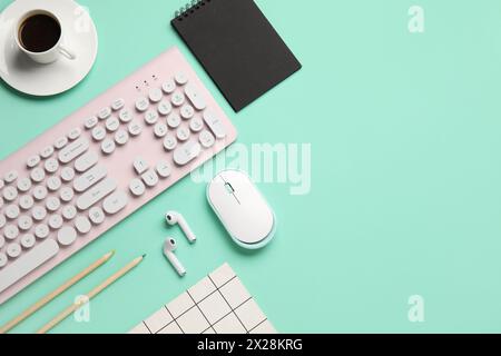 PC keyboard, mouse, earphones, coffee and stationery on turquoise ...