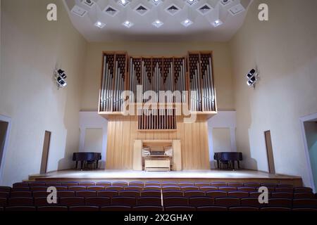 Massive wooden pipe organ in empty large concert hall; rows of seats ...