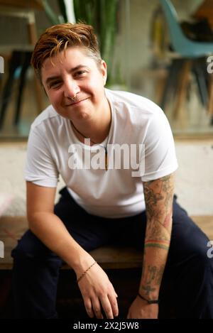 Smiling young transgender professional sits comfortably in modern ...