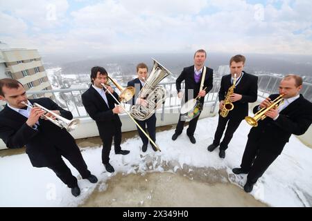 Brass band of six musicians play on roof of tall building at winter ...