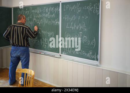 Teacher writes mathematics formulas on blackboard in school classroom ...
