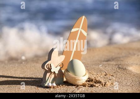 Toy bunny, surfboard and painted Easter egg on sea beach Stock Photo ...