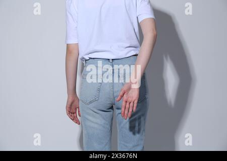 Woman showing open palm behind her back on grey background, back view ...