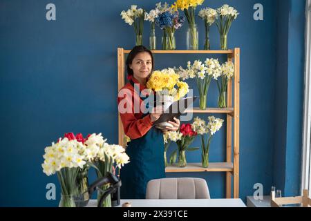 A female florist holds a bouquet and makes notes on a clipboard while ...