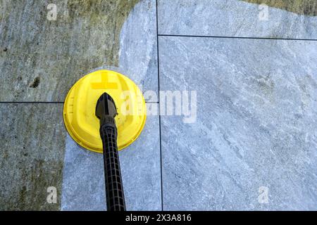 Pressure jet washer being used to clean porcelain tiles on a garden ...