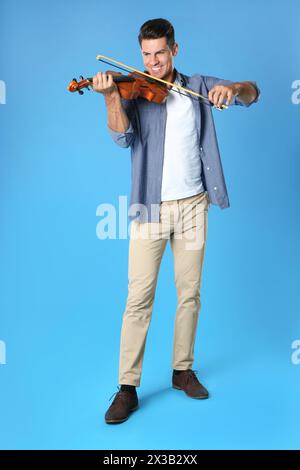 Happy man playing violin on light blue background Stock Photo - Alamy