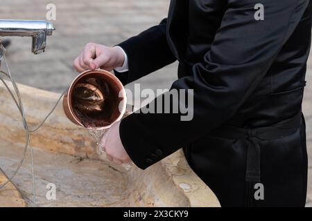 Closeup of a man using a copper natla or Jewish ritual hand washing cup ...