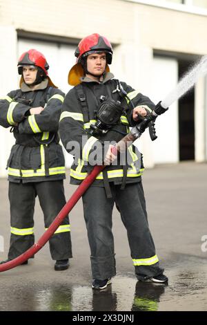 Portrait of two heroic fireman holds and adjust nozzle and fire hose ...