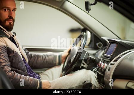 Bearded man sits on driver seat in car at underground parking, view ...