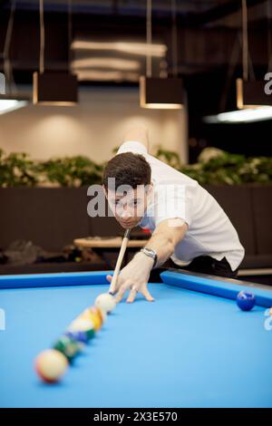 Man in white polo-neck shirt chalks tip of cue stick standing near pool ...