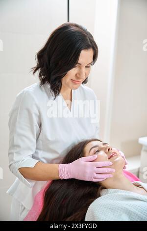 Woman therapist performing a facial massage on a female client lying on ...