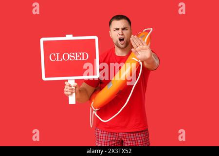 Shouting young lifeguard with lifebuoy and sign "closed" on red ...