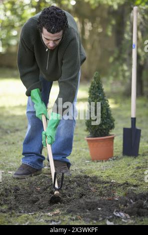 Man digging soil with a hoe in a garden Stock Photo - Alamy