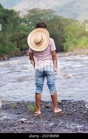 Man standing barefoot on rocks beside a flowing river in a natural ...