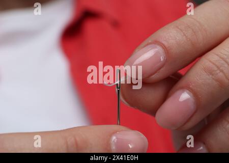 Woman inserting thread through eye of needle on blurred background ...