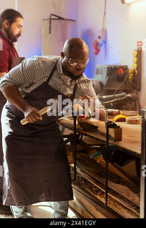 Artisan next to BIPOC coworker using sanding block to remove imperfections on wood piece ...