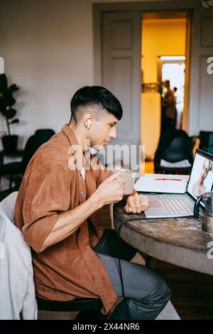 Mid adult male freelancer with coffee cup working on laptop in cafe ...