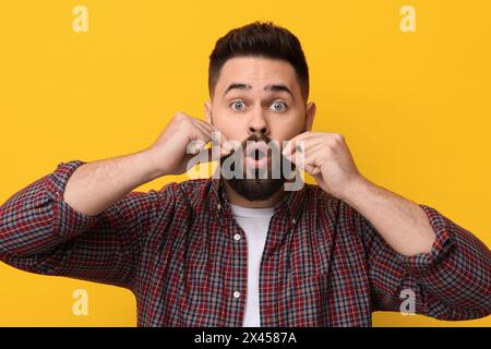 Surprised young man touching mustache on light blue background Stock ...
