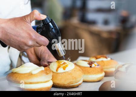 Unrecognizable crop chef caramelizing sugar cream on sweet Berliners ...