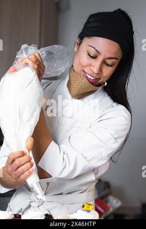 Female happy baker squeezing whipped cream from pastry bag on tasty ...