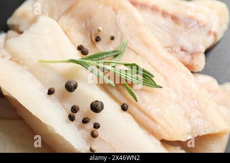 Pieces of raw cod fish, rosemary, peppercorns and lemon on grey table ...