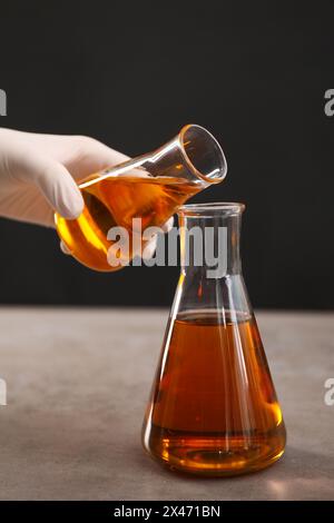 Woman pouring yellow crude oil into flask at grey table against dark ...