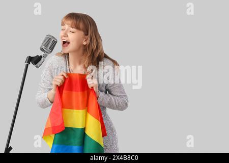Female artist with LGBT flag and microphone singing on light background ...