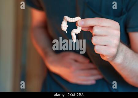 Man holding a miniature intestine model in one hand while clutching his ...