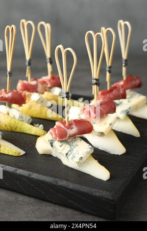 Tasty canapes with pears, blue cheese and prosciutto on grey table ...