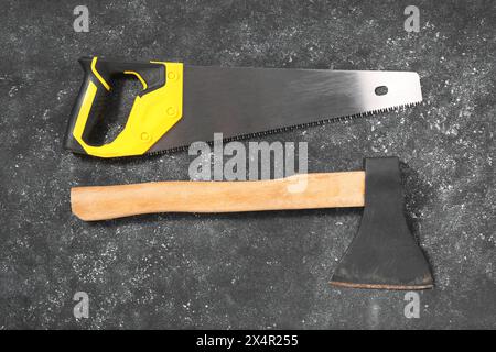 Saw with yellow handle and axe on dark gray textured background, flat ...