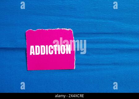 Addiction word written on ripped blue paper piece with brown background ...
