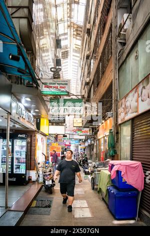 Looking down a tight packed alley with small shops, markets stalls and ...
