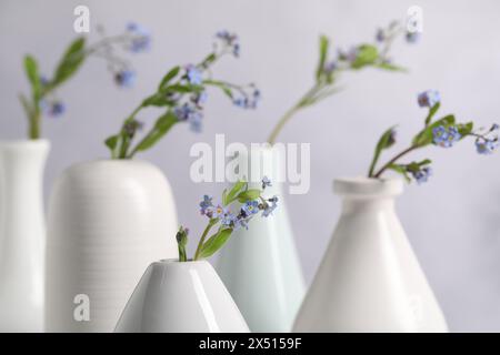 Beautiful forget-me-not flowers in vases on white marble table, closeup ...