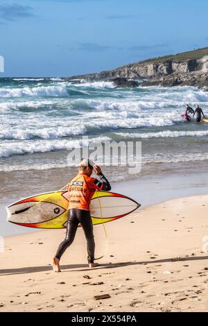 A young Grom surfer carrying his surfboard walking along the shoreline ...