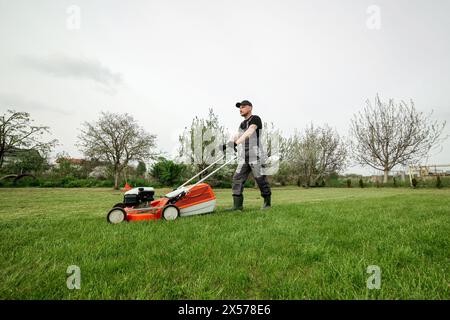 Professional gardener in protective apparel is mowing green grass lawn ...